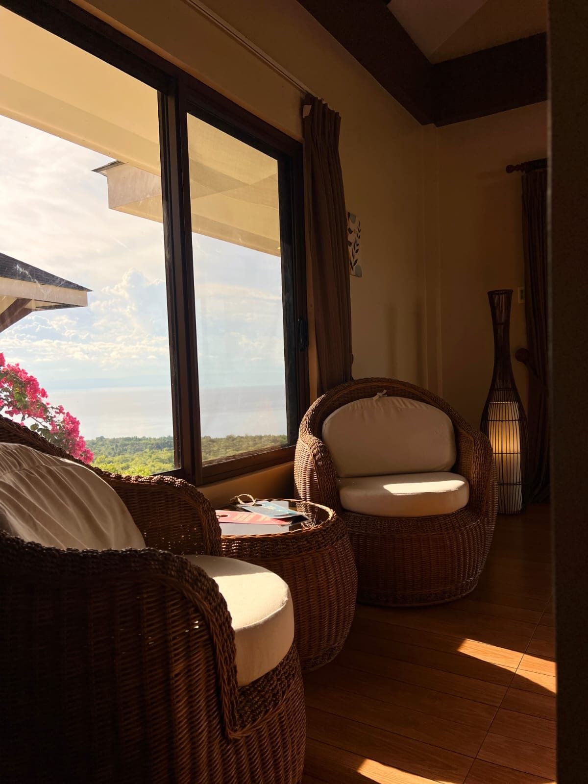 Quarto com mobiliário de vime, vista para o mar e uma grande janela.