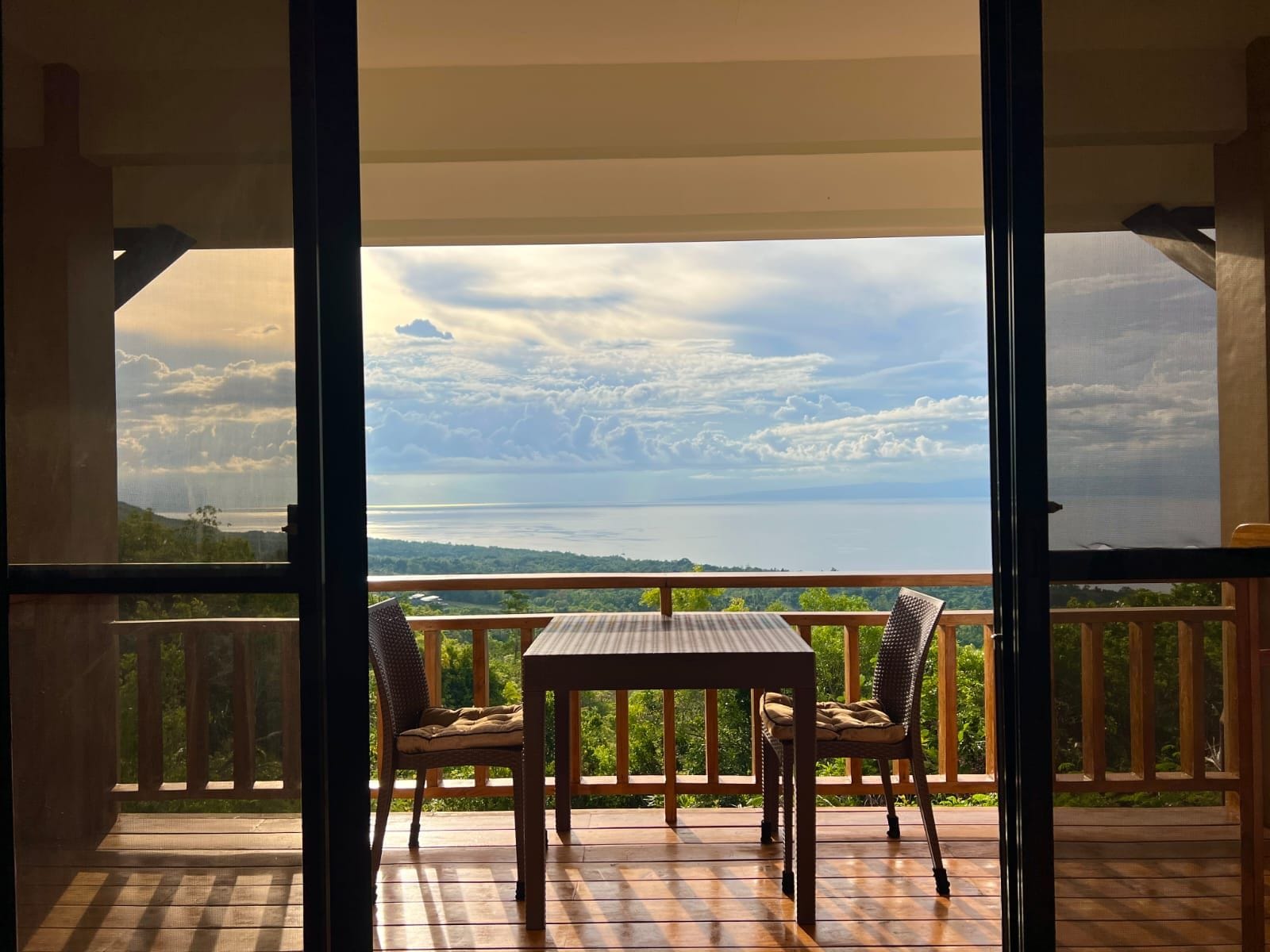 Um deck de madeira com uma mesa e duas cadeiras, com vista para uma paisagem deslumbrante de um corpo d'água e terras distantes.