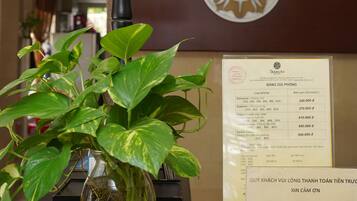 Um balcão de recepção com uma luminária, um vaso de planta e um quadro de cardápio.