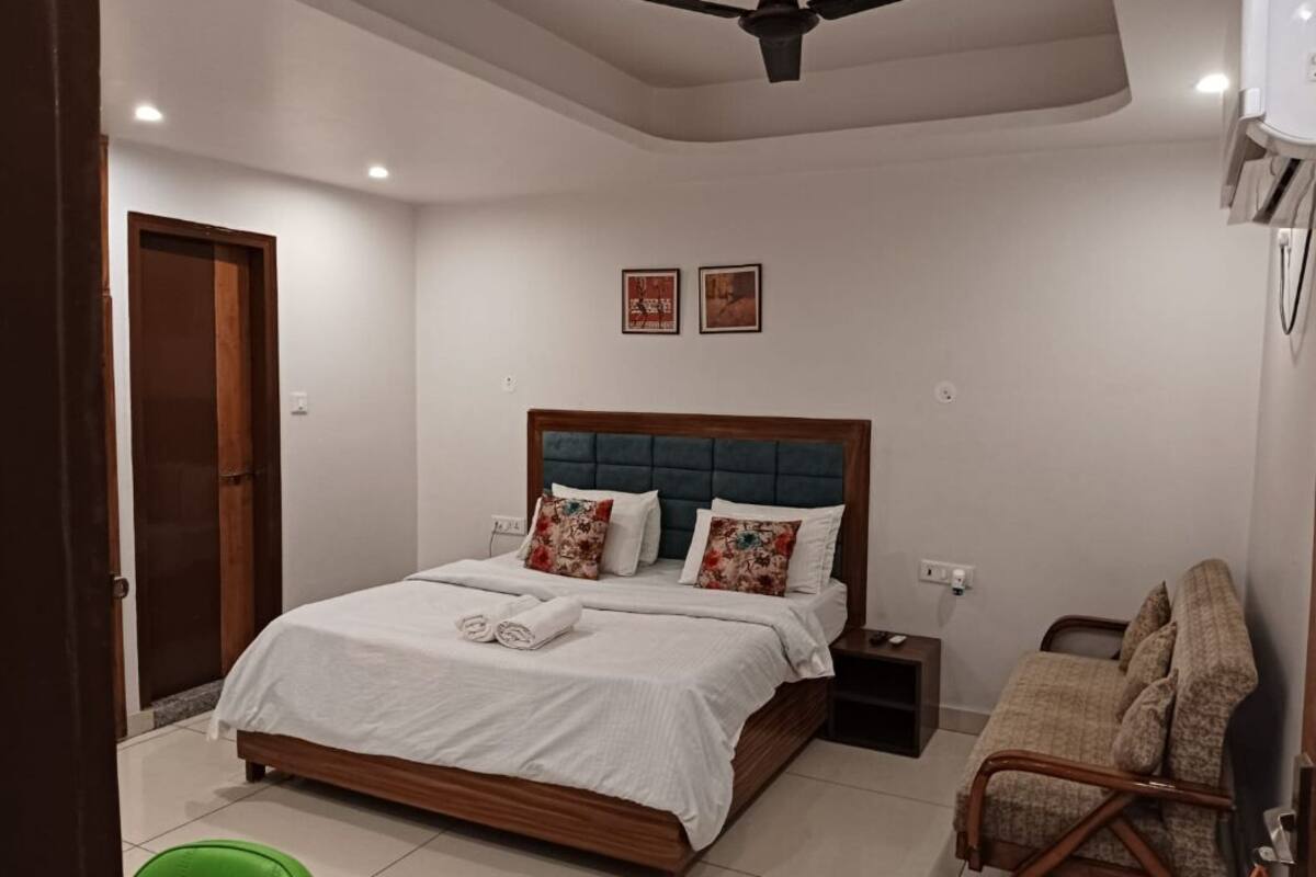 Quarto com cama, uma cadeira, ventoinha no teto e dois aparelhos de ar condicionado fixados na parede.