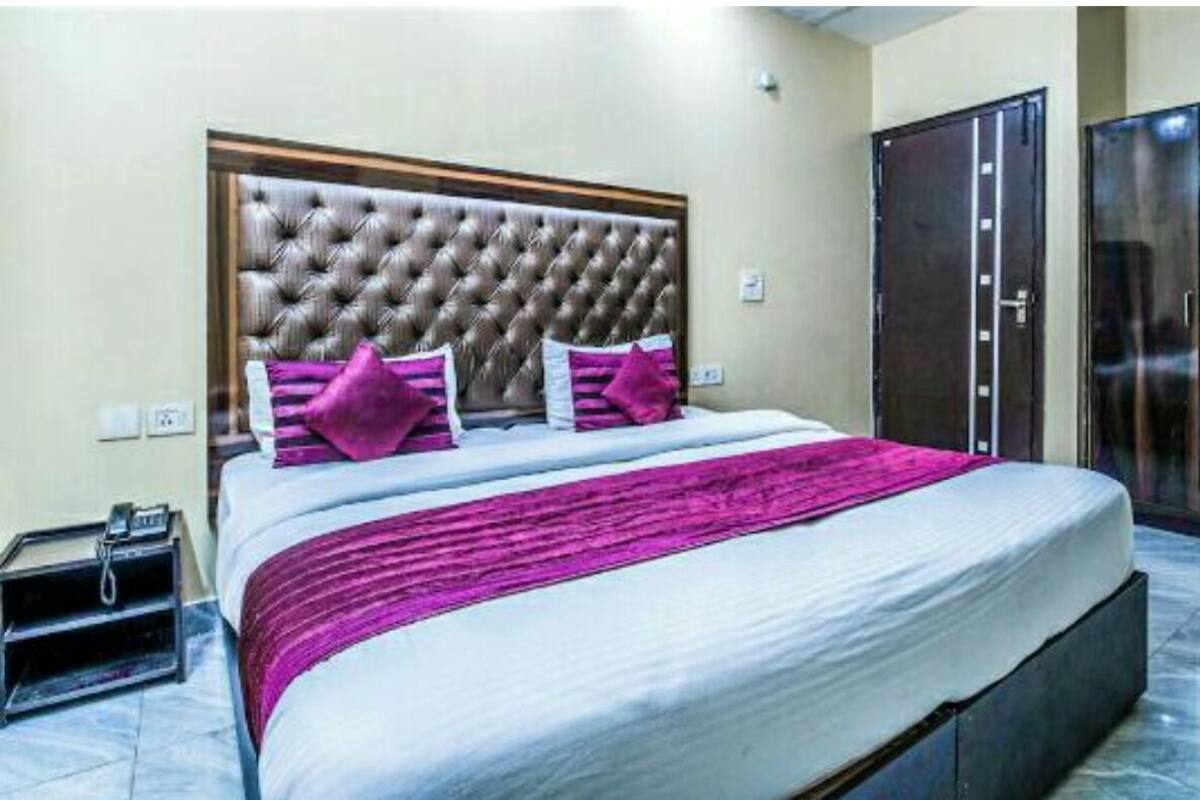 Quarto de hotel com uma cama grande, cabeceira, guarda-roupa e mesa de cabeceira.