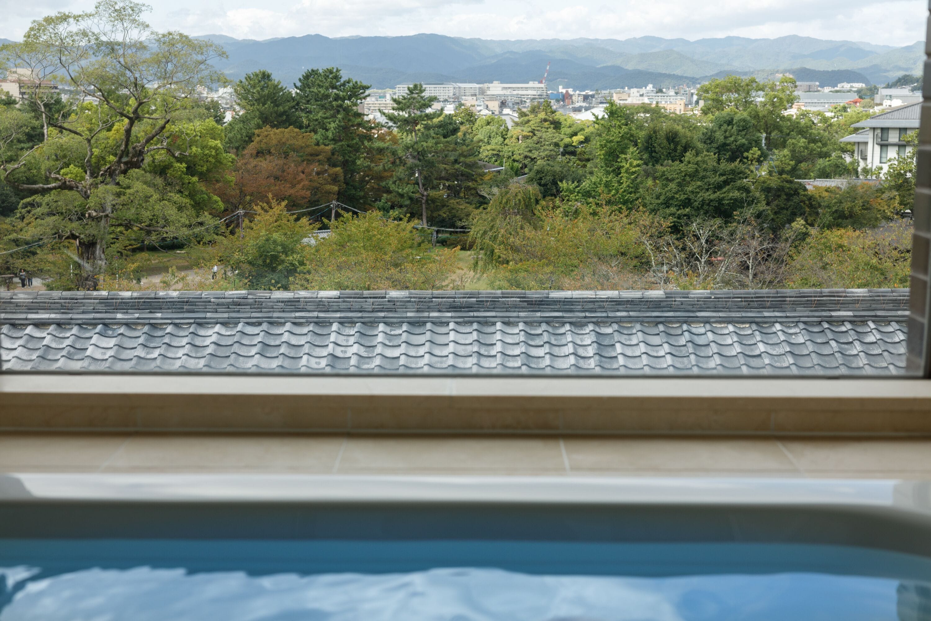Vista da janela com vista para uma piscina, com telhado telhado e árvores ao primeiro plano.