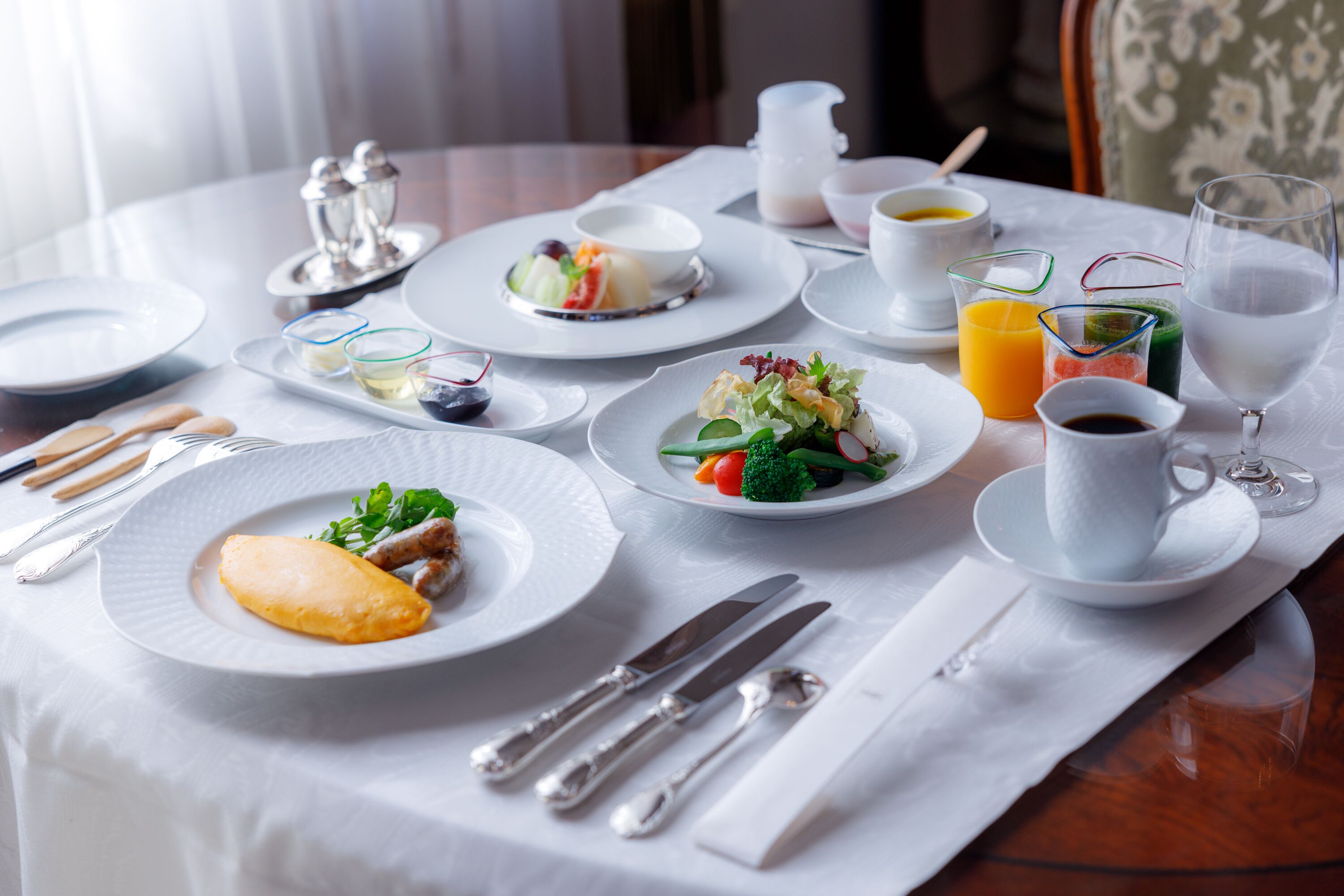 Uma mesa de pequeno-almoço posta com pratos, talheres e bebidas.