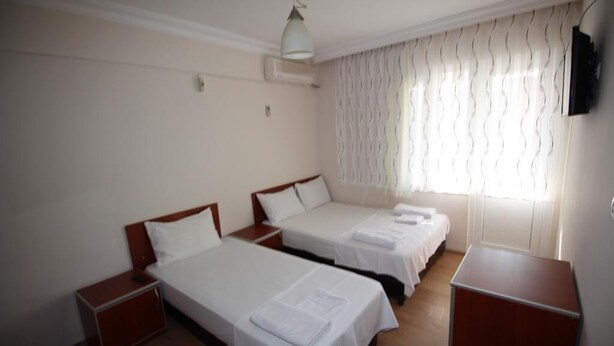 Quarto de hotel com duas camas de solteiro, mesa de cabeceira de madeira, escrivaninha e janela com cortinas.