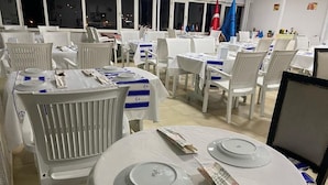 Uma área de refeições com mesas redondas, cadeiras brancas e bandeiras.