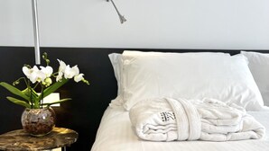 Cama bem arrumada com toalha dobrada, um vaso com flores brancas e chuveiro moderno.