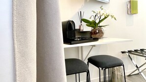 Quarto moderno com televisão de tela plana na parede, uma mesinha com uma planta, duas cadeiras pretas e um espaço compacto para passar roupa.