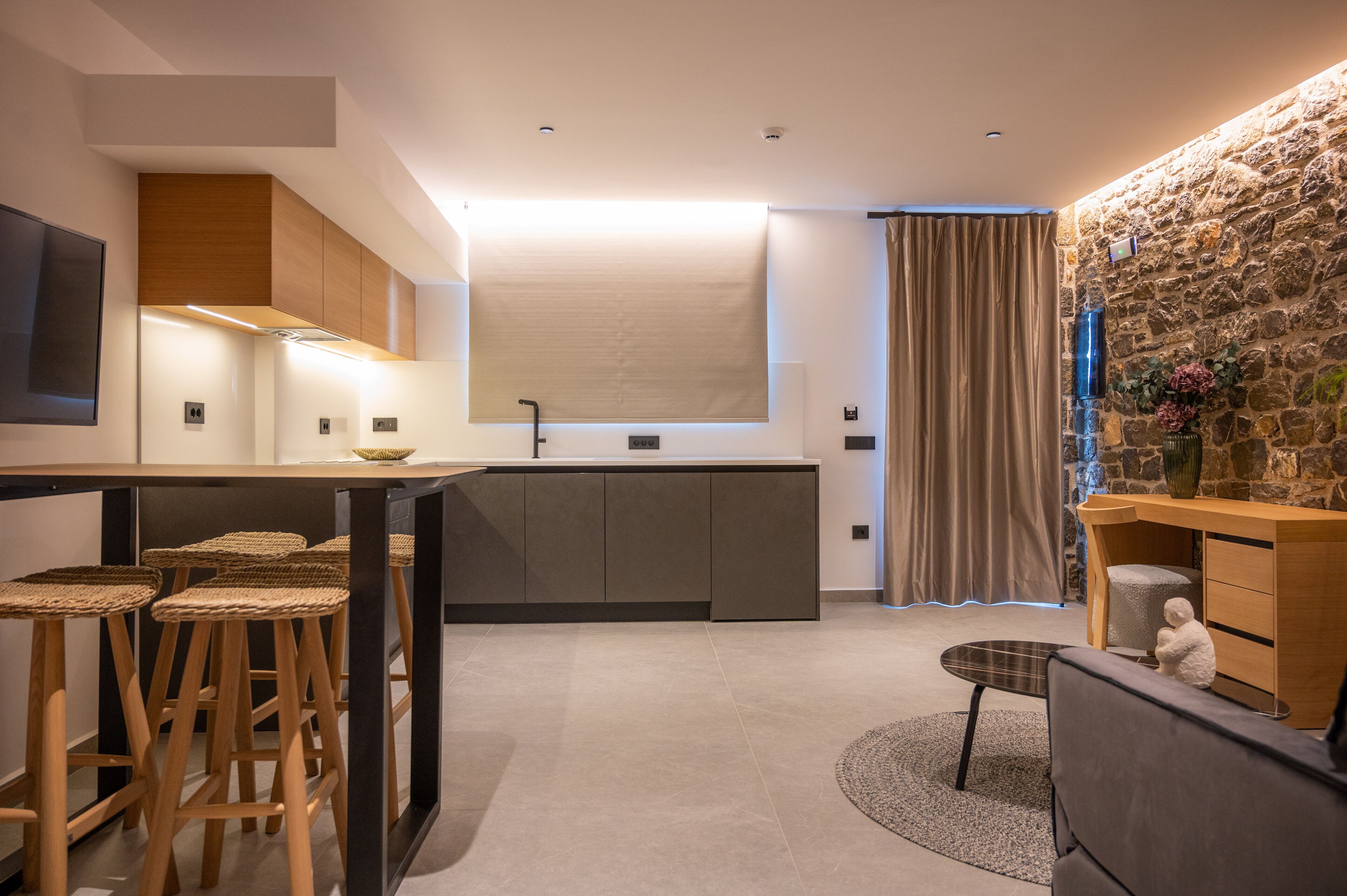 Cozinha moderna com ilha central, banquetas e parede decorada com pedra.