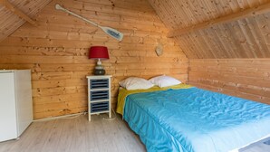 Quarto de cabana de madeira com uma cama, uma luminária vermelha, uma prateleira branca na parede e uma geladeira branca.
