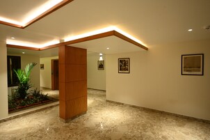 Um corredor com um pilar de madeira, soalho em mármore e quadros nas paredes.