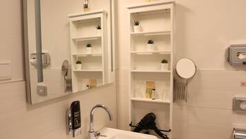 Uma casa de banho com uma pia branca, espelho, prateleiras com produtos de higiene pessoal e um tapete de banho azul.