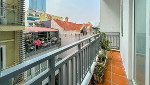 Varanda com guarda-corpo, plantas em vasos e vista para edifícios vizinhos.