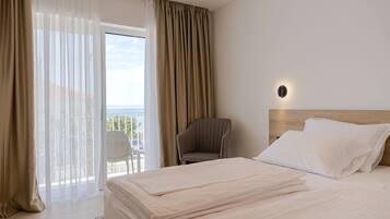 Quarto de hotel com cama, cadeira, varanda e vista, e luminária na parede.