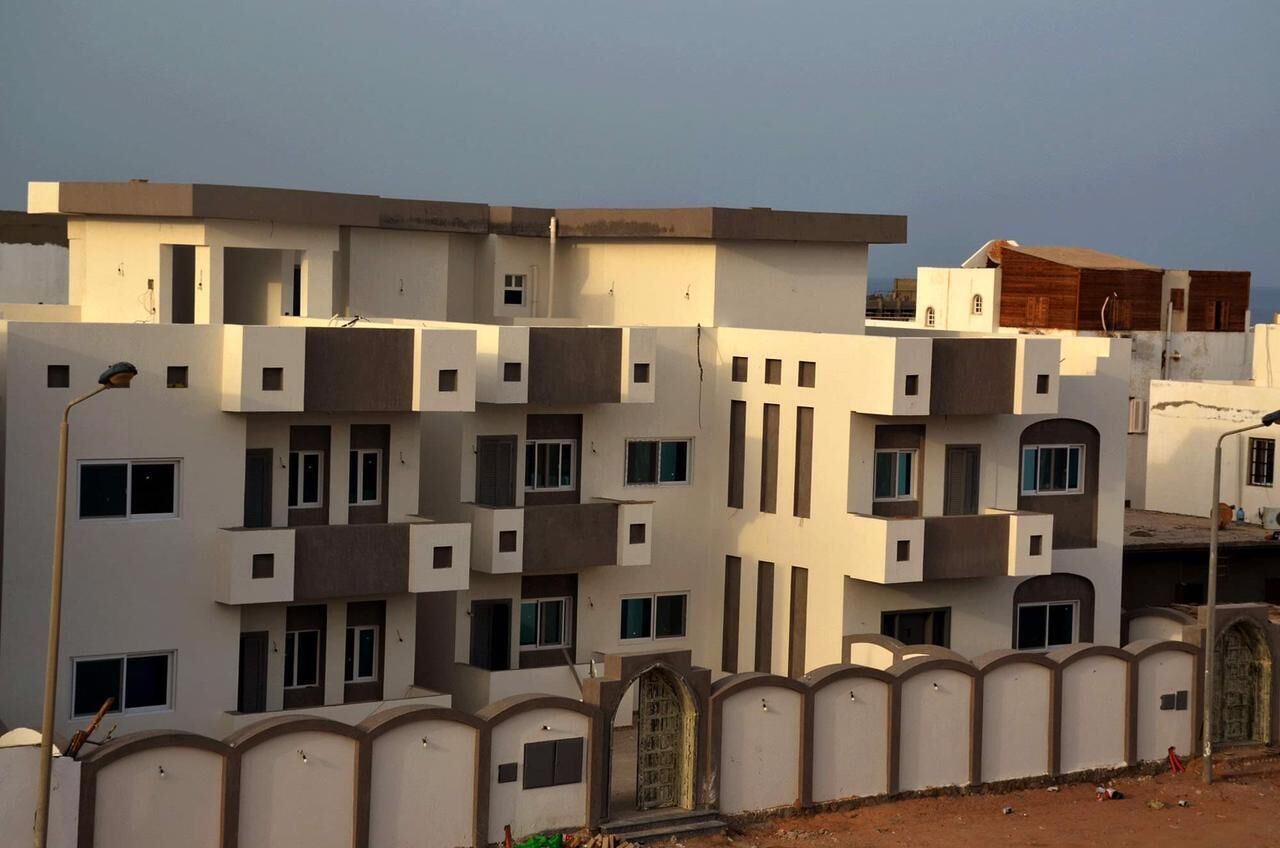 Um edifício residencial com vários andares, design arquitetônico moderno, com varandas e portão fechado.