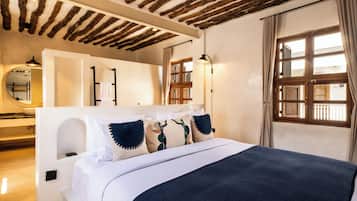 Quarto com cama grande, vigas de madeira no teto, janela com cortinas e um espelho na parede.