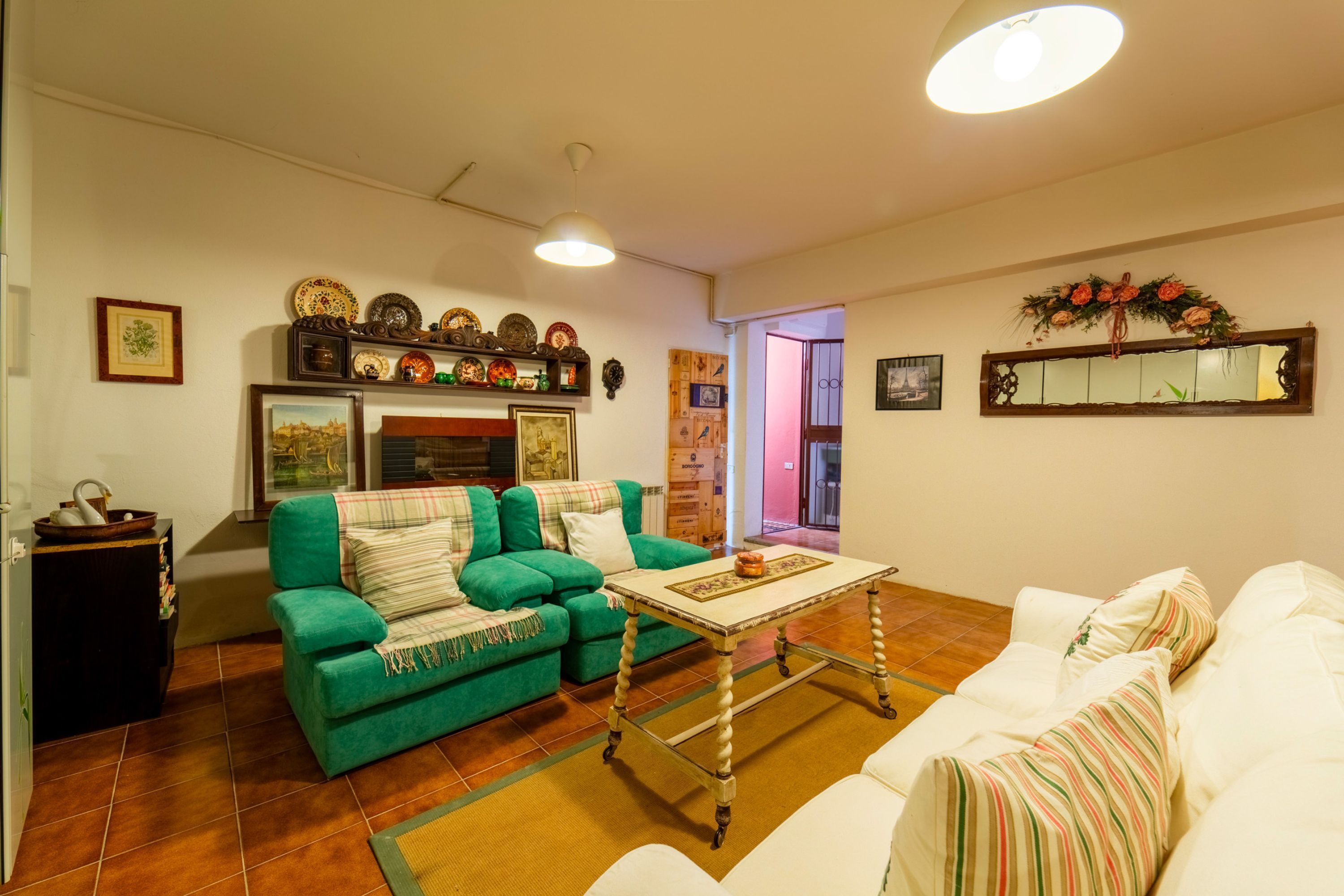 Sala de estar com um sofá verde-água, um sofá branco e uma mesa de centro de madeira. Há decorações nas paredes e um espelho sobre os sofás.