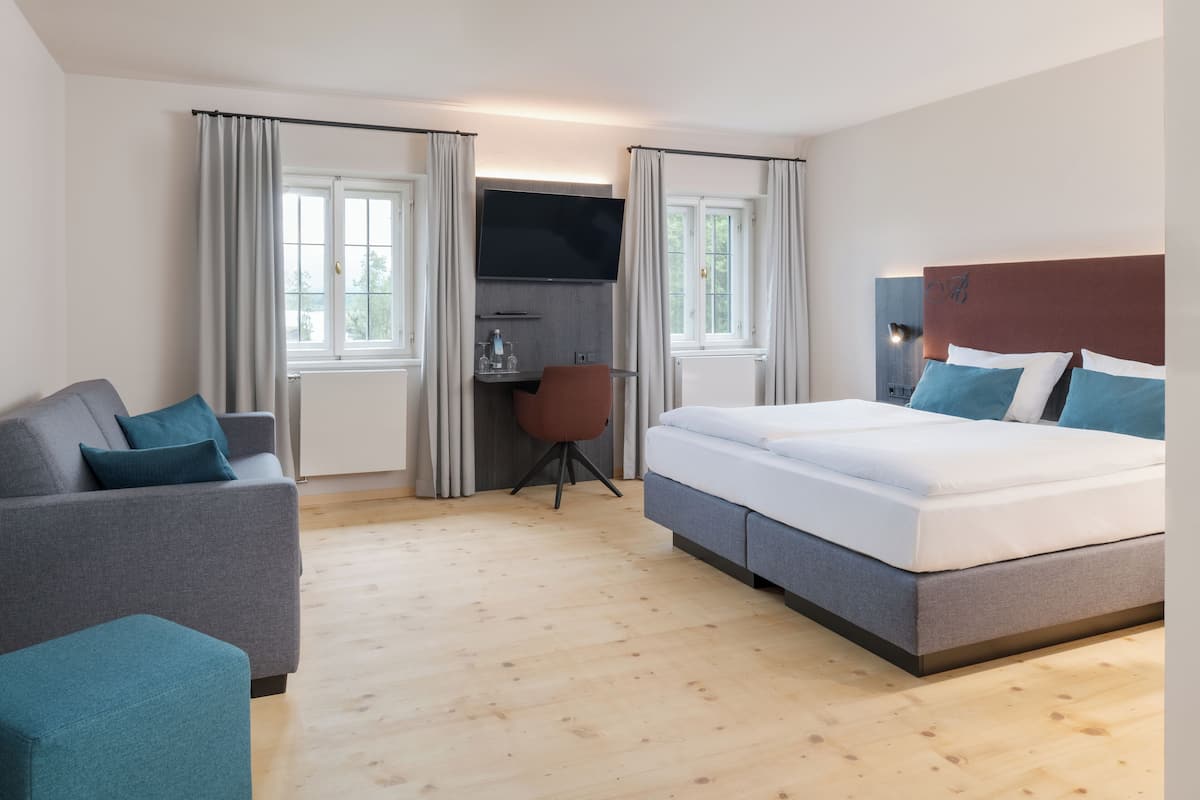 Quarto de hotel moderno com cama, sofá, escrivaninha e televisão.