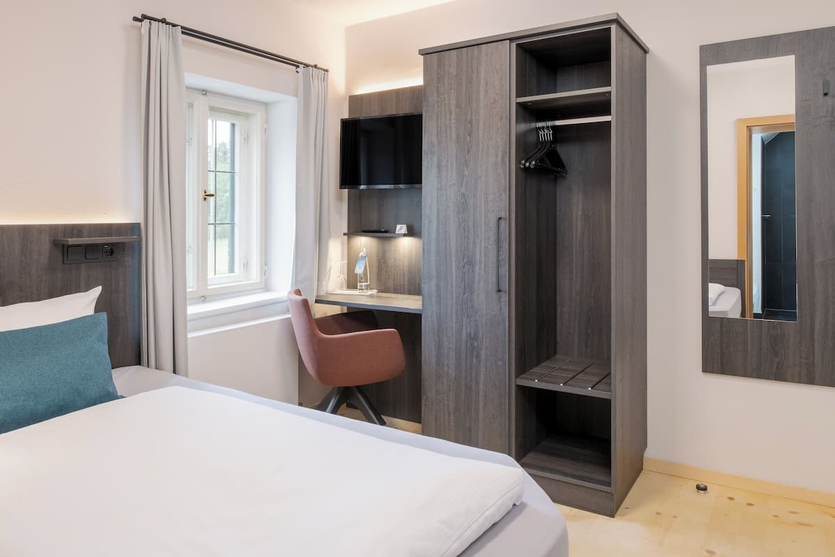 Quarto de hotel moderno com cama, escrivaninha, cadeira, guarda-roupa e espelho.
