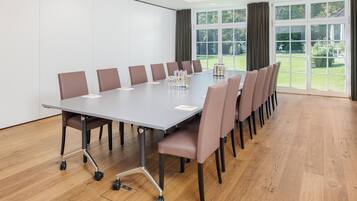 Sala de conferências com uma longa mesa, cadeiras e vista para um jardim através de amplas janelas.