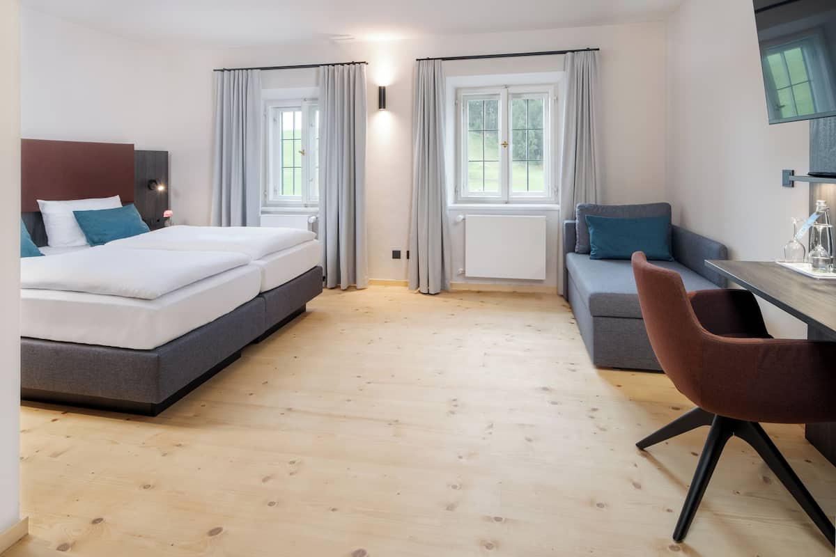 Quarto de hotel moderno com duas camas, um sofá, uma escrivaninha e uma cadeira.