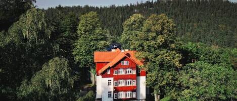 Um edifício de vários andares com telhado vermelho, rodeado por uma floresta densa.