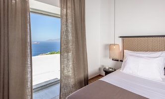 Quarto de hotel com cama, mesa de cabeceira, luminária e vista para o mar.