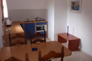 Uma cozinha compacta com forno embutido, pia e pequena mesa de jantar com cadeiras.