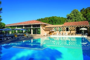 Piscina com espreguiçadeiras e guarda-sóis, cercada por edifícios com telhados de telha vermelha.