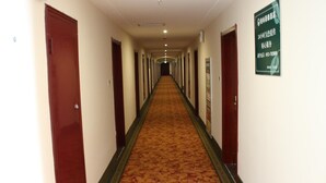 Corredor longo e estreito de hotel, com portas em ambos os lados e piso coberto de carpete.
