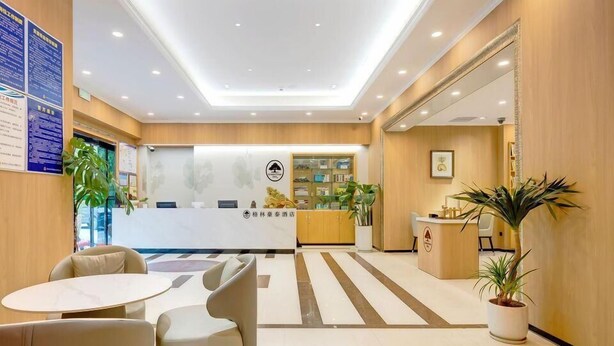 Uma área de recepção de hotel moderna, com balcão de atendimento, espaço para sentar e plantas em vasos.