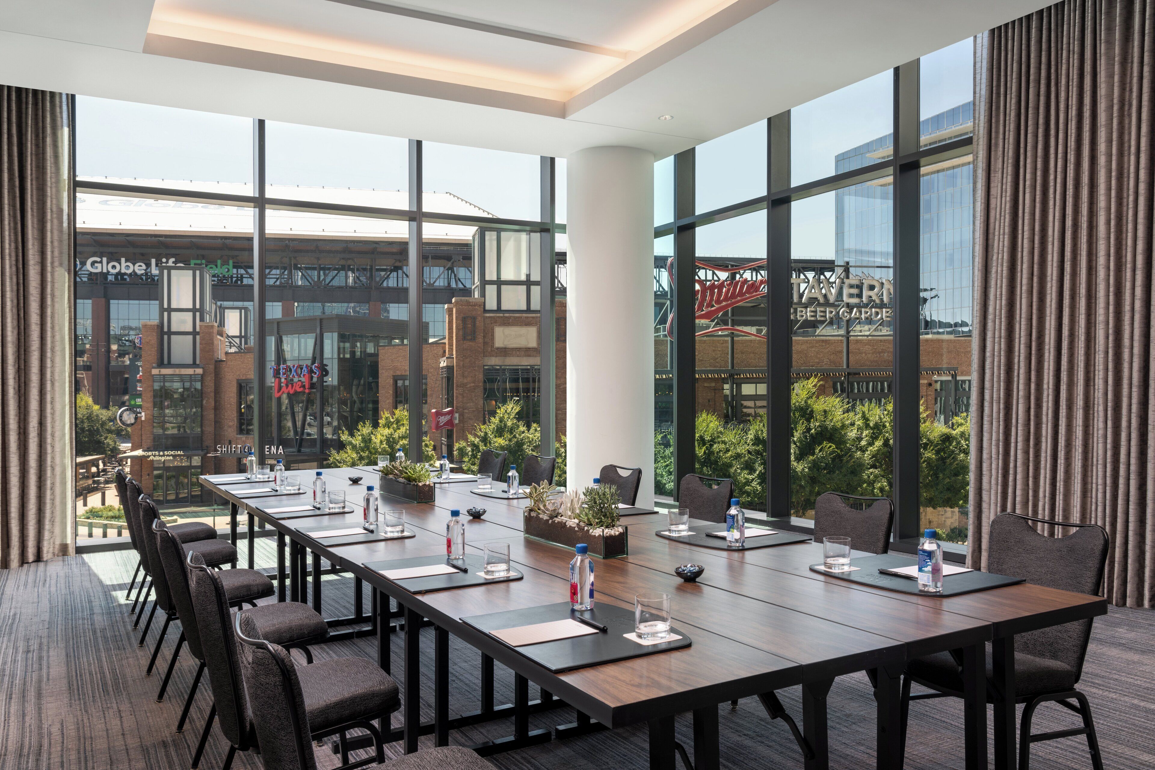 Sala de conferências com uma mesa comprida, cadeiras, garrafas de água e vista para um edifício com um letreiro.