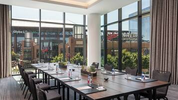 Sala de conferências com uma mesa comprida, cadeiras, garrafas de água e vista para um edifício com um letreiro.