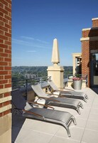 Terraço no telhado com espreguiçadeiras e um obelisco decorativo, com vista para a paisagem urbana.