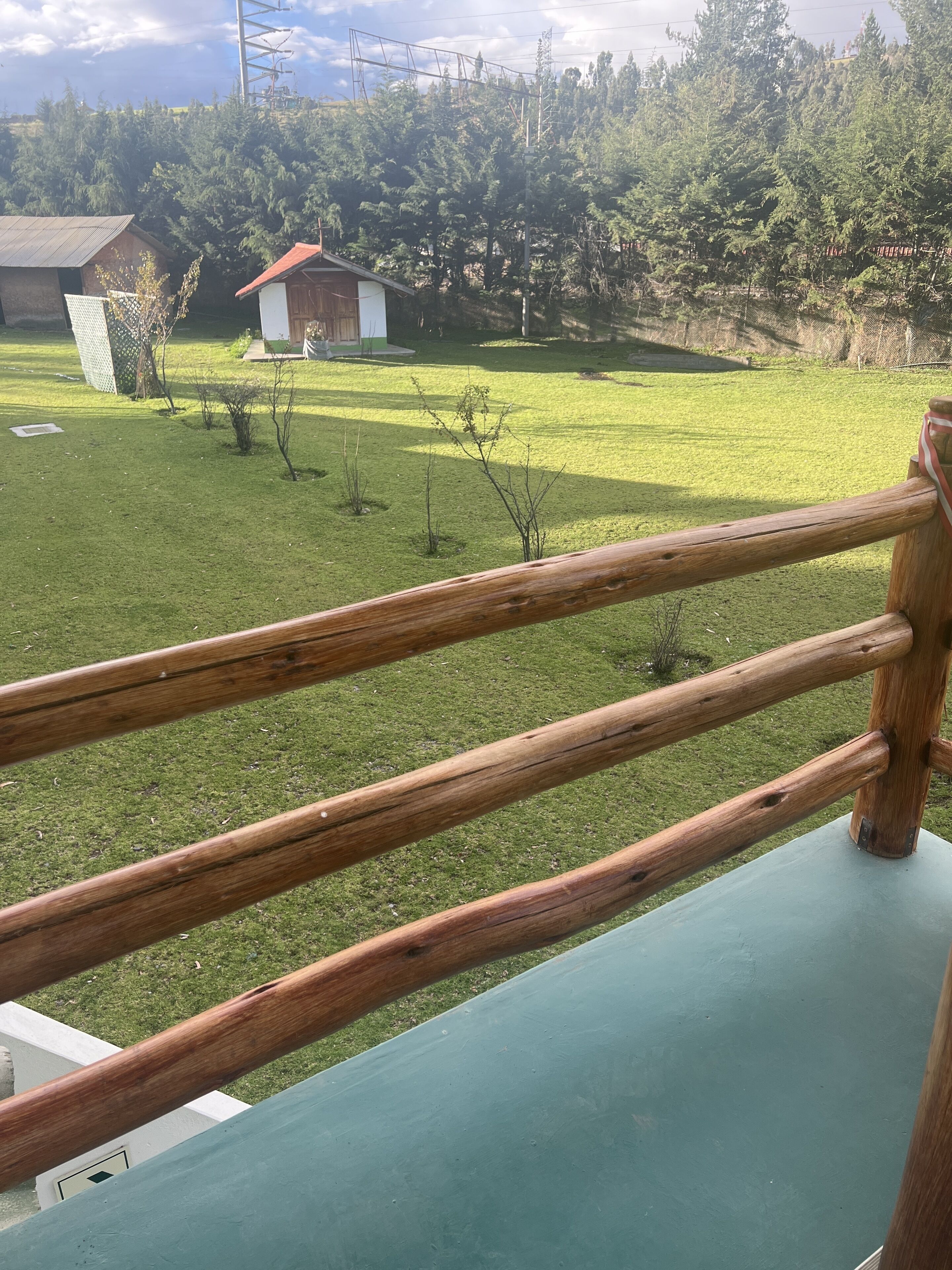 Guarda de madeira com vista para um jardim bem cuidado e um pequeno edifício ao fundo.