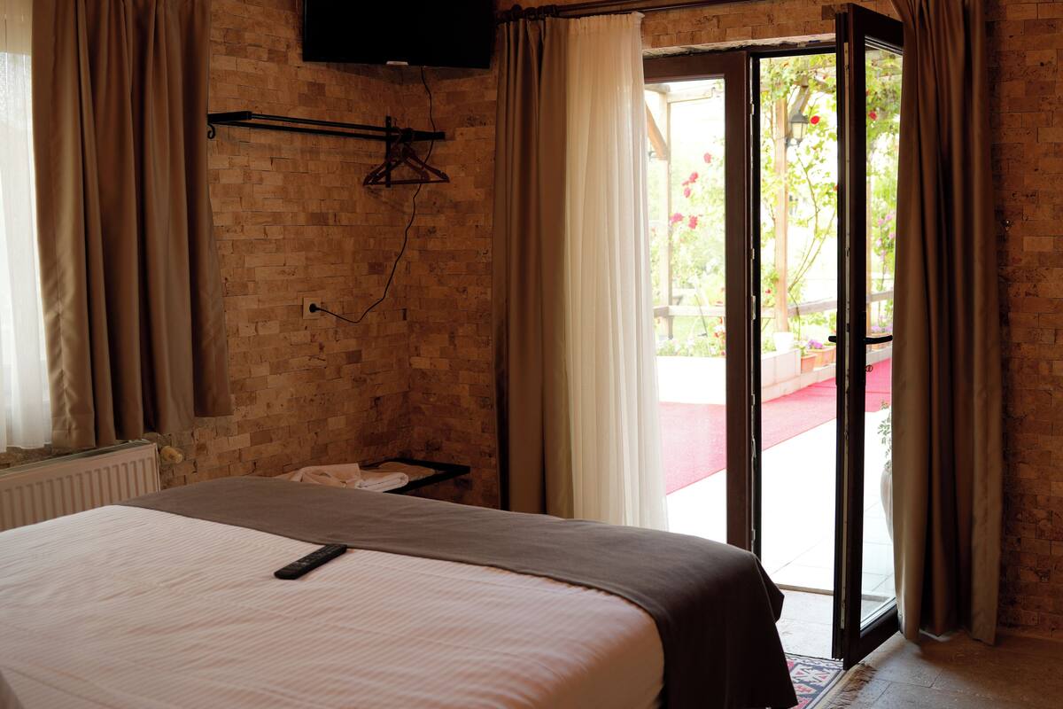 Quarto de hotel com uma cama, televisão fixada na parede e porta de vidro deslizante para área externa.