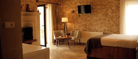 Quarto de hotel com parede de tijolos, lareira, cama, poltrona, mesa com abajur e TV fixada na parede.