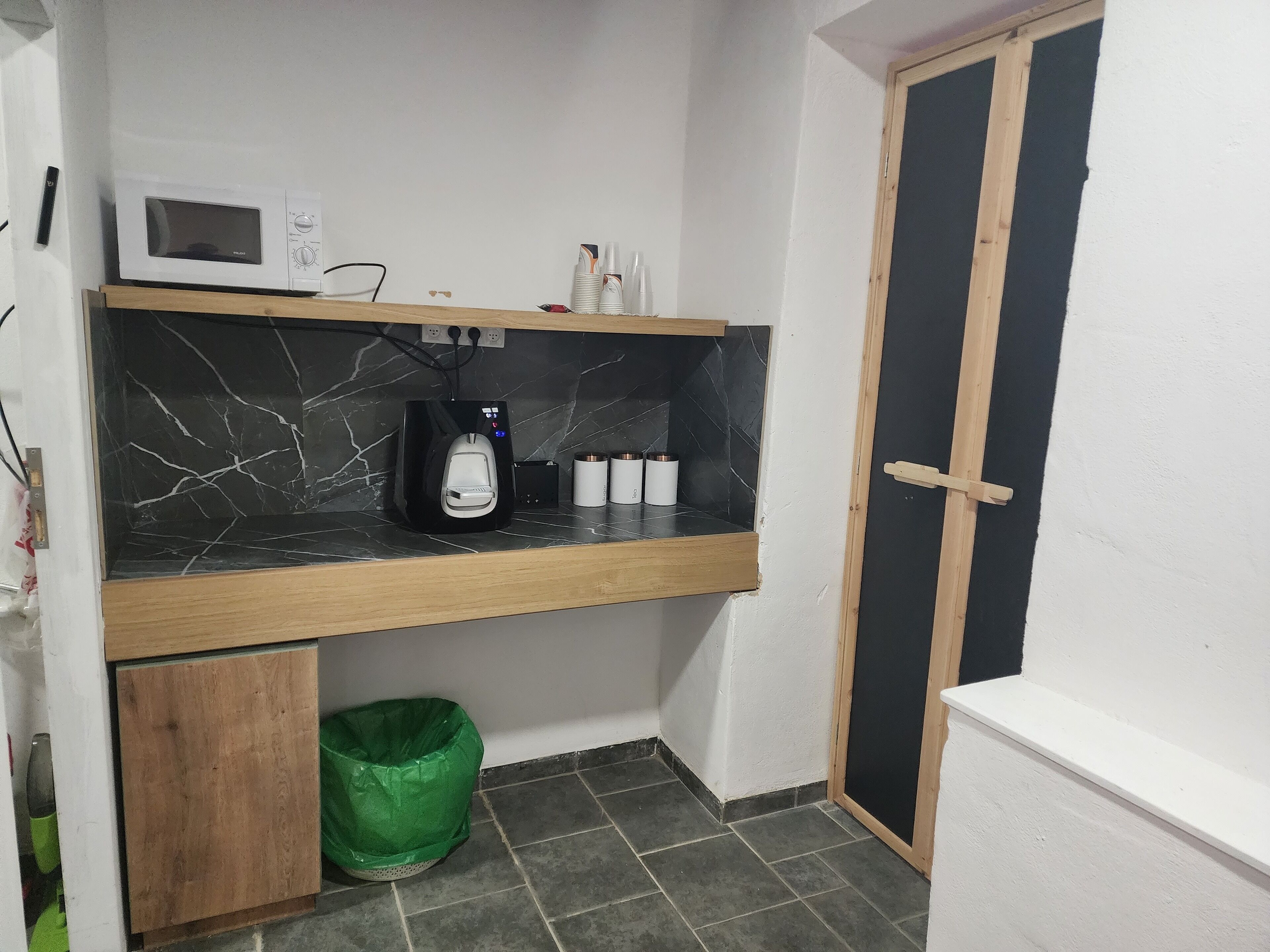 Cozinha compacta com micro-ondas, máquina de café e xícaras empilhadas em bancada de mármore preto.