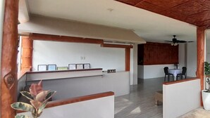 Um quarto amplo com teto de madeira, uma mesa de recepção, uma área de refeições com mesa e cadeiras e um ventilador de teto.
