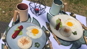 Duas travessas de comida com ovos e arroz, uma caneca e uma vela sobre uma mesa ao ar livre.