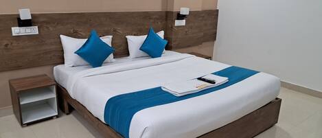 Uma cama bem arrumada com roupa de cama branca e azul, uma cabeceira de madeira e uma mesa de cabeceira com abajur.