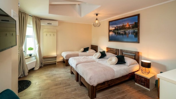 Quarto de hotel com duas camas, piso de madeira, pintura de uma paisagem urbana e mesa de cabeceira com luminária.