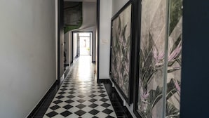 Um corredor com chão xadrez, obras de arte nas paredes e uma porta no final que dá para o exterior.