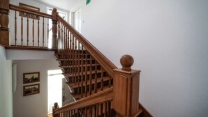 Uma escada de madeira com corrimão e balaústres, que dá acesso a um andar superior.