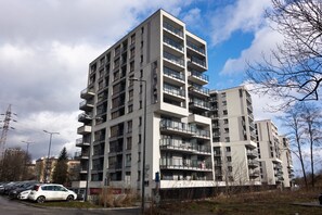 Um edifício residencial de vários andares com varandas, área de estacionamento e céu claro.