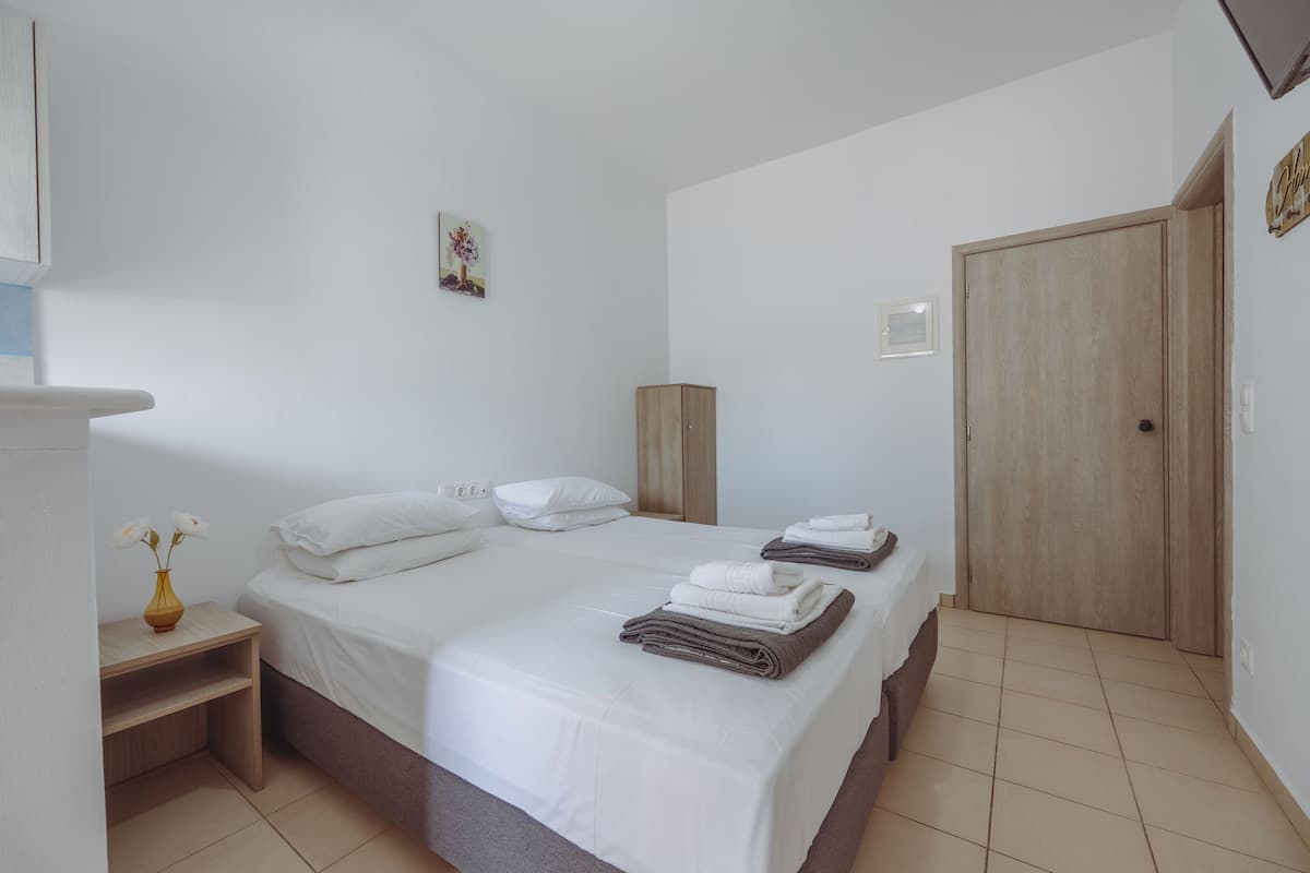 Quarto de hotel com uma cama, mesa de cabeceira, guarda-roupa de madeira e uma pequena mesa com um vaso.