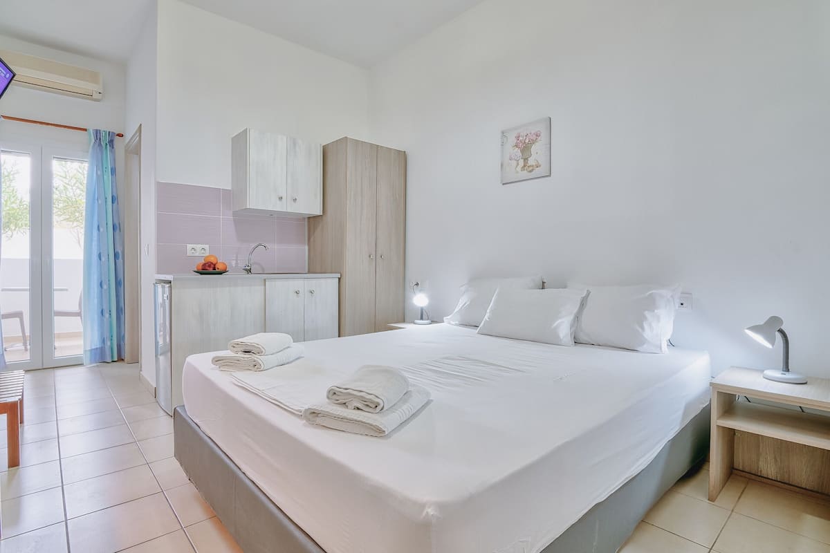 Quarto de hotel com cama, escrivaninha, mesa de cabeceira, pequena cozinha e banheiro.