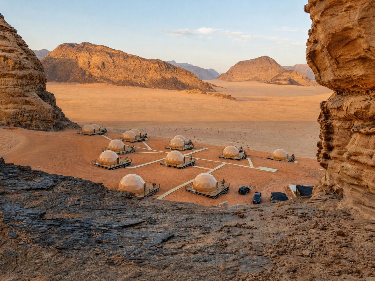 Paisagem desértica com várias estruturas em forma de cúpula dispostas em padrão de grade, cercada por terreno rochoso e montanhas ao longe.