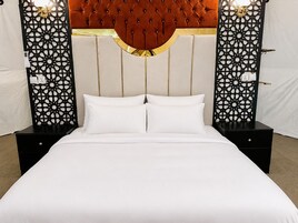 Uma cama com cabeceira estofada, duas mesas de cabeceira e painéis decorativos em ambos os lados.