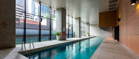 Piscina interior com paredes de vidro transparente, chão revestido e placa indicando 'proibido mergulhar'.