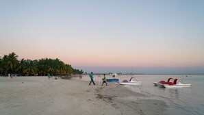 Uma praia com palmeiras, algumas pessoas e barcos na areia.